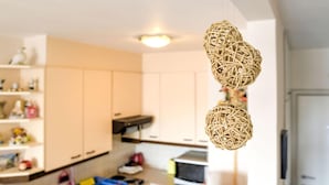 Cozinha com armários brancos, micro-ondas e luminária pendente de fibra natural.
