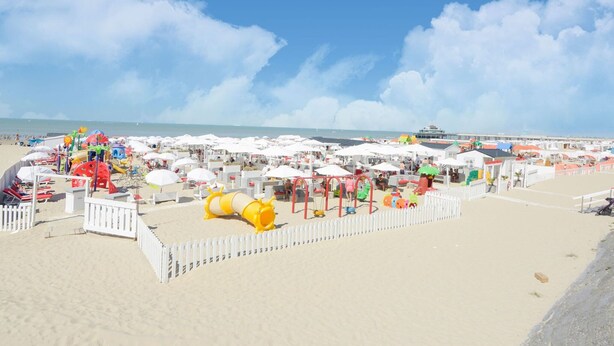 Uma praia com guarda-sóis brancos e uma área de recreação cercada.