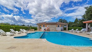 Uma piscina com espreguiçadeiras, um pequeno edifício com telhado de azulejos e céu claro.