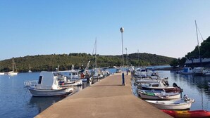 Uma marina com barcos atracados ao longo de um cais de concreto, cercada por água e uma encosta arborizada.