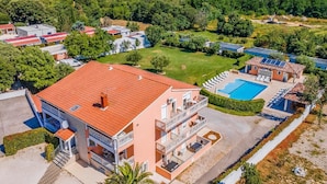 Um edifício de vários andares com telhado de telhas vermelhas, piscina e jardim ajardinado.