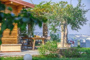 Uma cabana de madeira com mesa e cadeiras, rodeada por vegetação e vista para a paisagem.