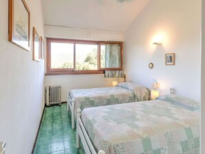 Quarto com duas camas, um radiador, janela com cortinas e quadros nas paredes.