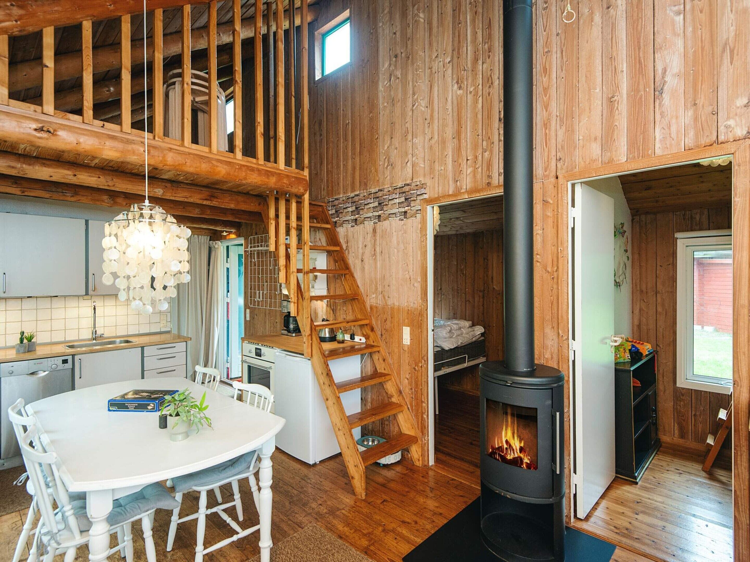 Um interior rústico com escada de madeira, área de jantar, cozinha e lareira a lenha.