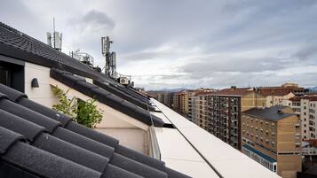 Terraço com telhado inclinado, antenas parabólicas e vista dos edifícios ao redor.