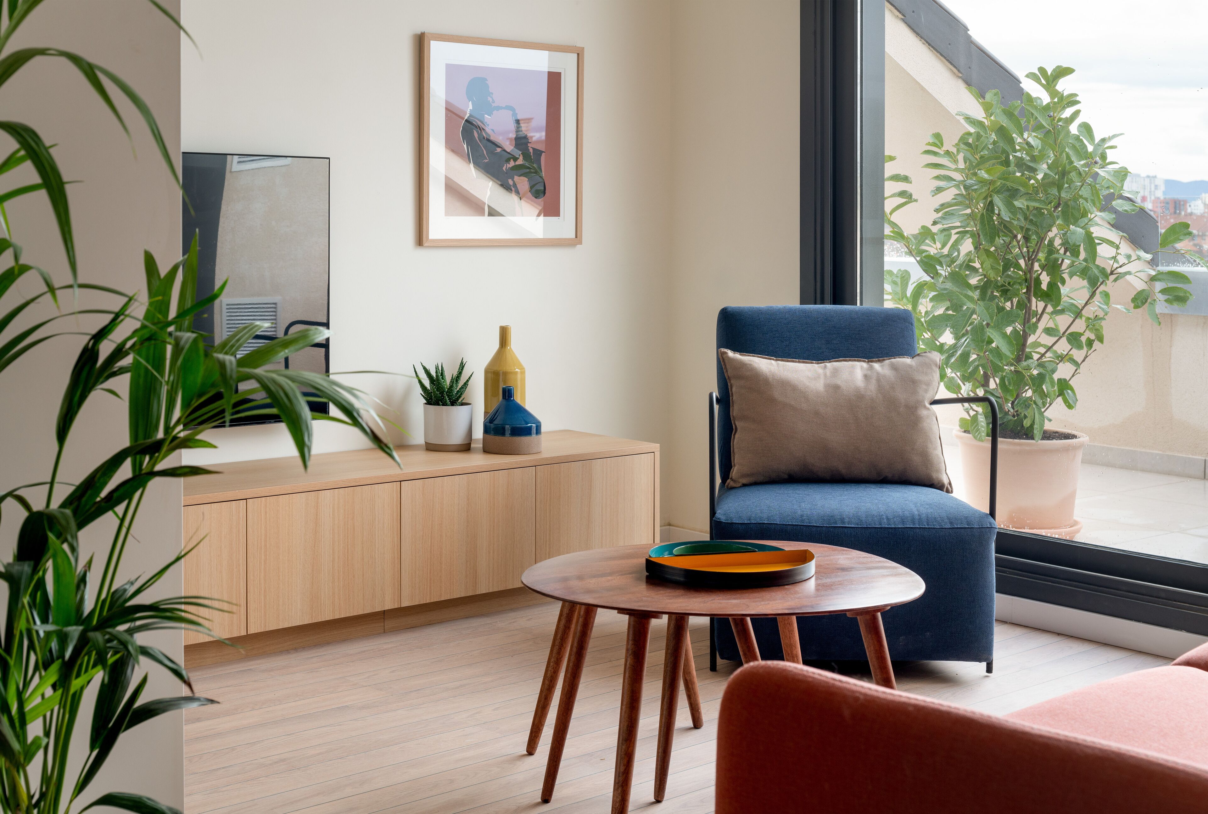 Uma sala de estar moderna com uma poltrona azul, uma mesinha redonda e um vaso de planta.