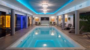 Piscina interior moderna com hidromassagem, espreguiçadeiras e um lustre no teto.