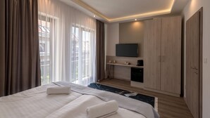 Quarto de hotel moderno com uma cama grande, televisão de tela plana, pequeno espaço de cozinha e um guarda-roupa.
