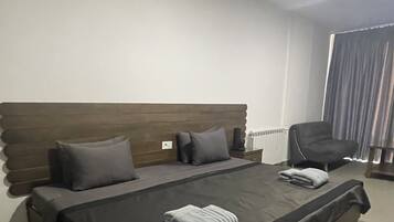 Quarto de hotel moderno com uma cama grande, cabeceira de madeira, uma cadeira e vista para o exterior.