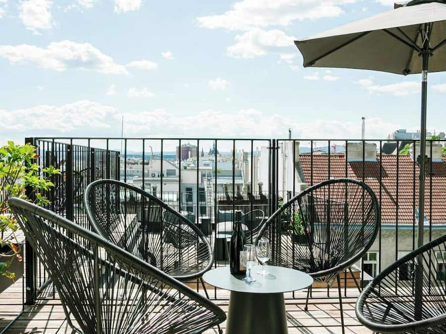 Terraço no telhado com mesa e cadeiras, vista para a paisagem urbana e grade de metal.