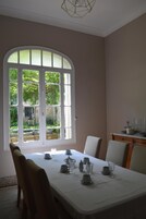 Uma área de refeições com uma grande janela em arco, uma mesa posta para quatro pessoas e um armário com utensílios de cozinha.