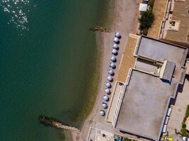 Vista aérea de um hotel à beira-mar, com uma linha de guarda-sóis e um edifício com telhado plano.