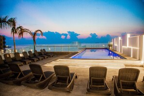 Área de piscina no terraço com espreguiçadeiras e guarda-corpo de vidro com vista para o mar.