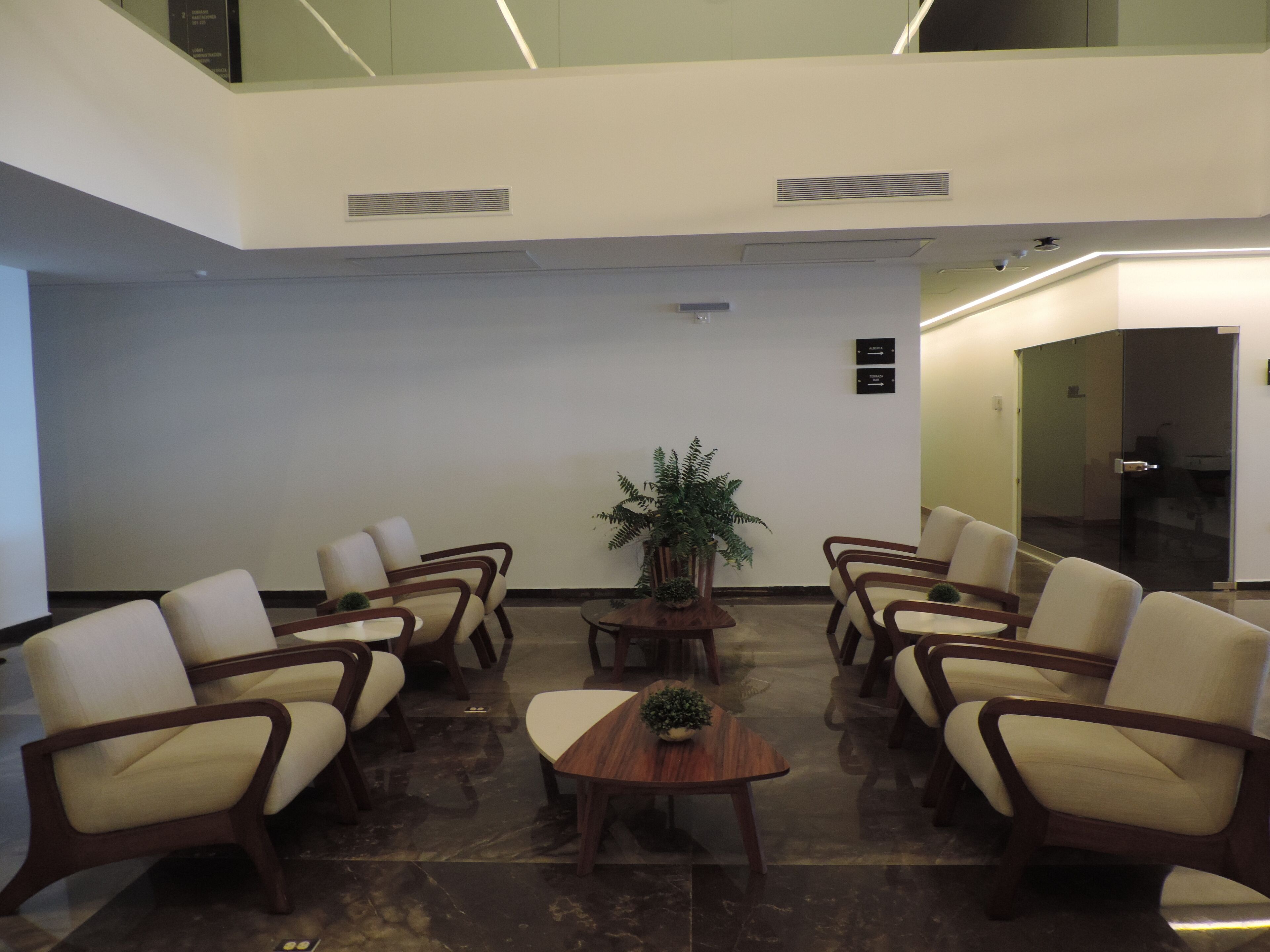 Um saguão com teto alto, uma planta central e uma área de estar com cadeiras e uma mesa.