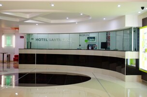 Uma área de recepção de hotel moderna, com fachada de vidro, balcão de atendimento e tela digital.