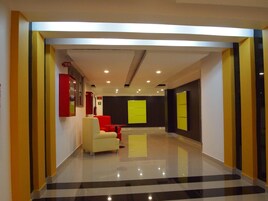 Um hall de hotel moderno com piso limpo e reluzente, uma poltrona vermelha e paredes com detalhes amarelos.