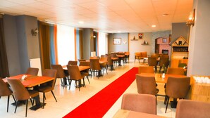 Uma área de refeições de hotel com várias mesas e cadeiras, um tapete vermelho e uma lareira de tijolos.