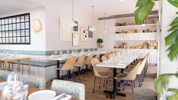 Restaurante com mesas comunitárias alongadas, cadeiras de vime e luminárias pendentes.