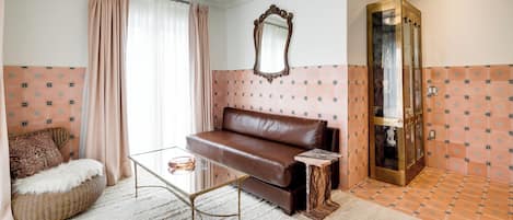 Um quarto com sofá de couro marrom, mesa de centro de vidro, cadeira de vime, espelho e papel de parede estampado.