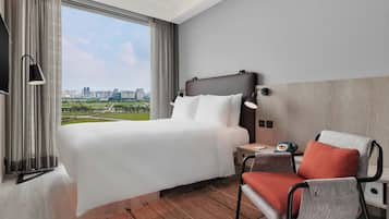 Quarto de hotel com uma cama grande, uma cadeira, uma mesa de cabeceira e vista para a cidade.