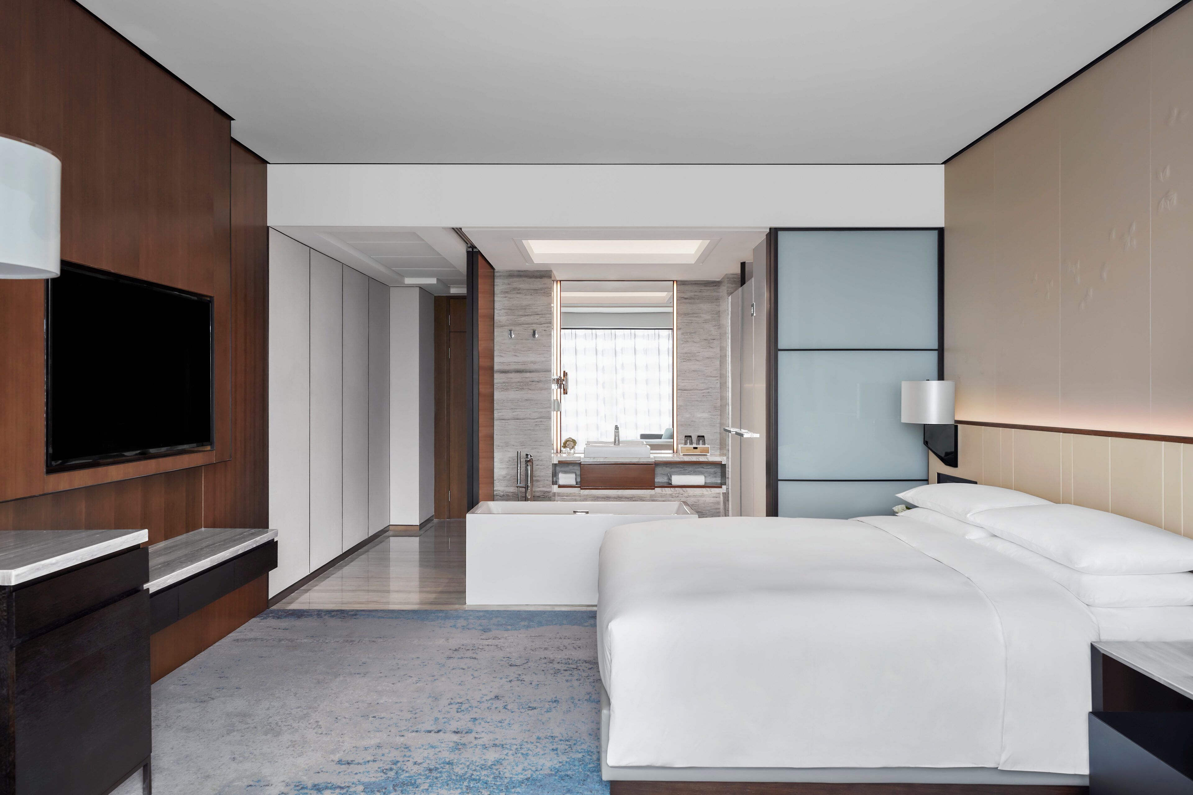 Quarto de hotel moderno com uma cama grande, televisão de tela plana na parede, banheiro com banheira e um closet espaçoso.