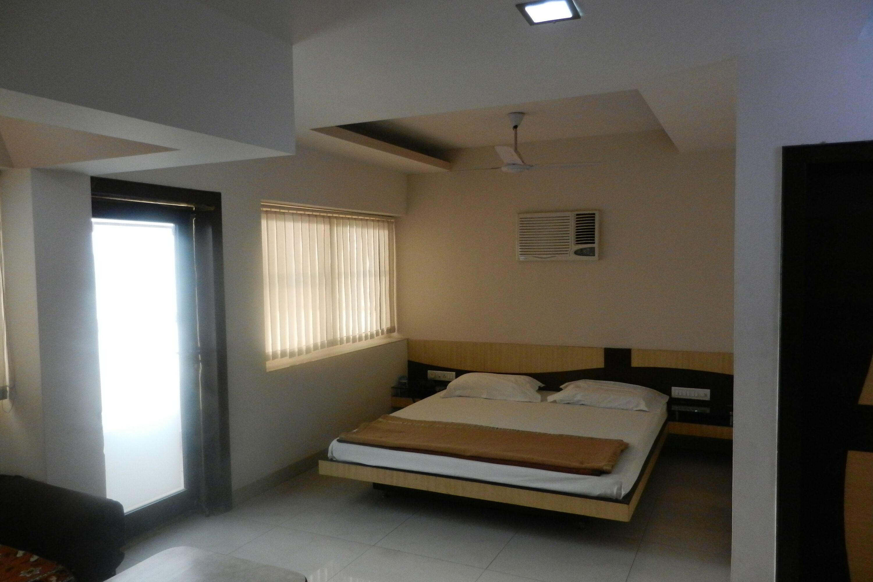 Quarto com cama, ventoinha no teto, janela com persianas e porta.