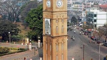 Um campanário com um relógio central e uma estátua na base, rodeado por uma praça circular com uma cerca.