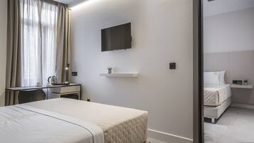 Quarto de hotel com cama, escrivaninha, cadeira, TV fixada na parede e uma pequena estante com uma planta.