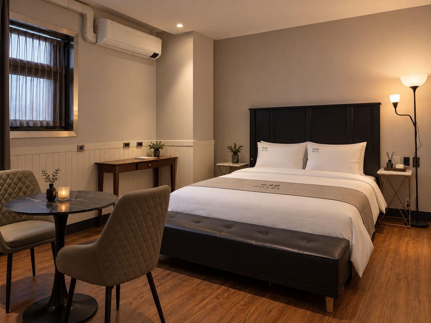 Quarto de hotel com cama, mesa de cabeceira, abajur, cadeira e uma pequena mesa com uma vela.