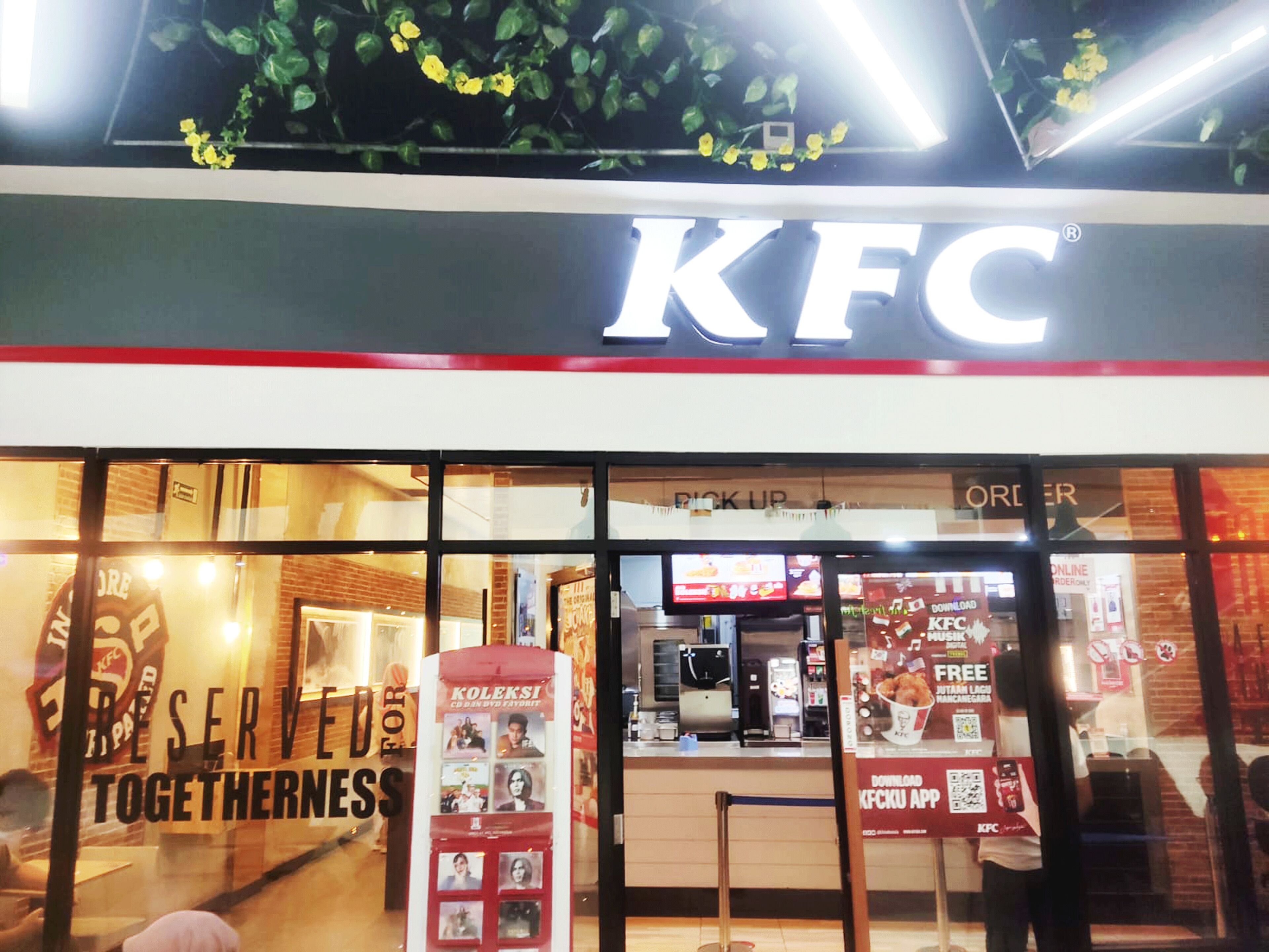 Um restaurante KFC com um letreiro que diz 'RESERVADO PARA ESTAR JUNTOS', um cartaz para baixar o aplicativo KFC e um letreiro que indica 'RETIRADA DE PEDIDO'.