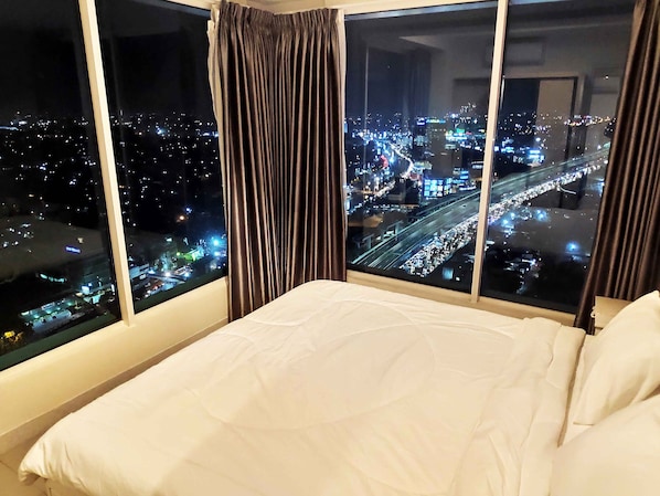 Quarto de hotel com uma cama grande e vista da cidade através de janelas do chão ao teto.