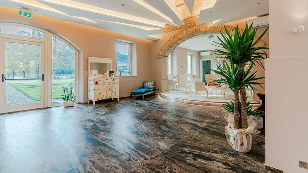 Um hall amplo com piso de mármore, janelas grandes, balcão de recepção e uma palmeira.