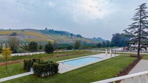 Uma piscina cercada por um gramado bem cuidado, com vista para colinas e algumas árvores ao fundo.