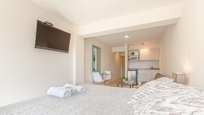 Quarto de hotel com cama, escrivaninha, cadeira e pequeno espaço de cozinha.