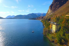 Um lago com um barco, edifícios numa encosta e montanhas ao fundo.