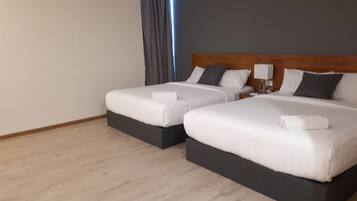 Quarto de hotel com duas camas, cabeceira de madeira, mesa de cabeceira e uma luminária.