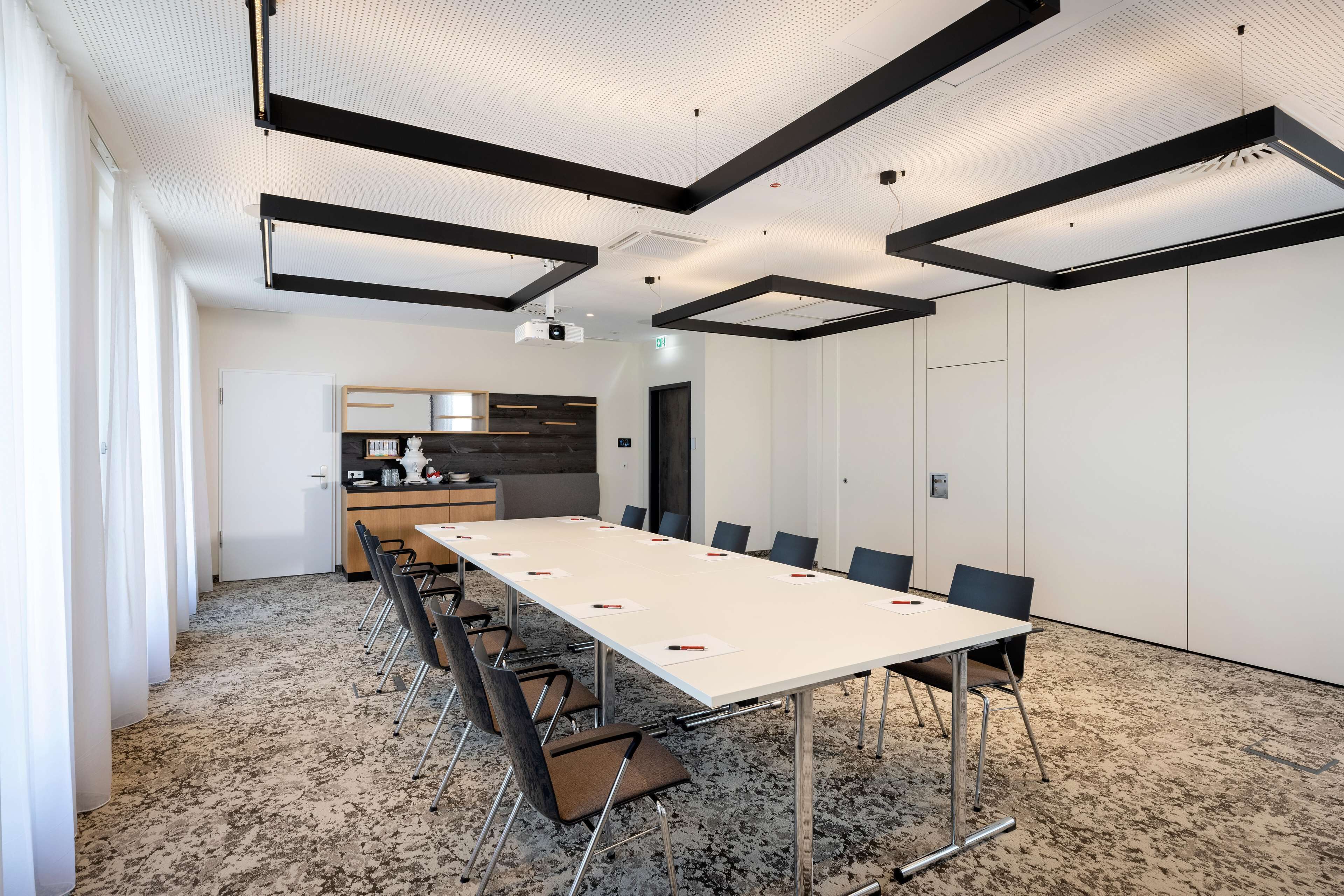 Uma sala de conferências com uma mesa comprida, cadeiras e uma área de cozinha ao fundo.