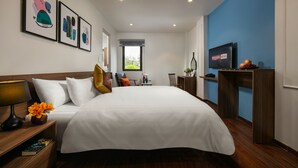 Quarto de hotel com uma cama grande, uma escrivaninha, uma televisão e obras de arte na parede.