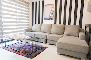 Uma sala de estar moderna com um sofá seccional, um tapete estampado, uma mesa de centro de metal e uma parede com listras verticais.