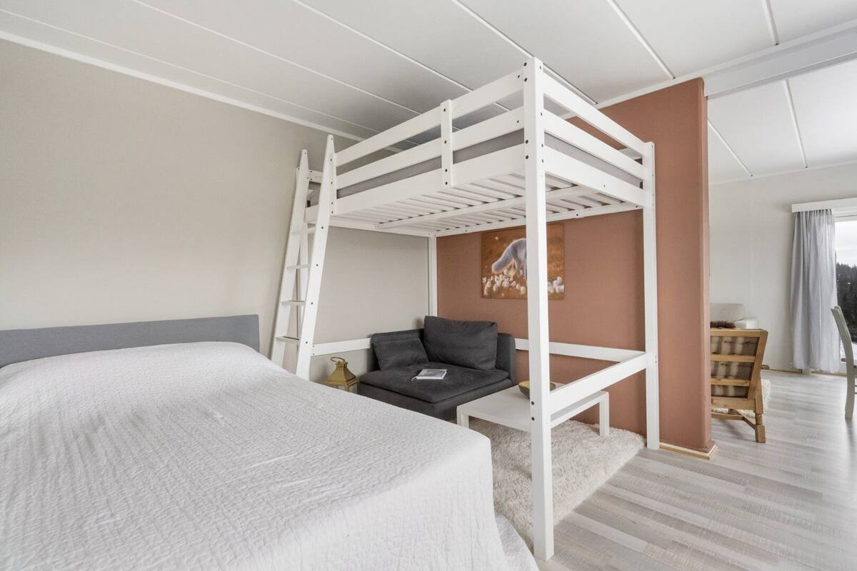 Uma cama beliche com escada, um sofá, uma mesinha e uma cadeira num quarto com vista.
