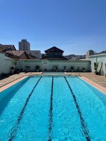 Piscina com água azul cristalina, cercada por um deck revestido e plantas em vasos.