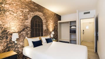 Quarto de hotel com uma cama grande, um guarda-roupa, uma mesa de cabeceira e uma parede com textura.