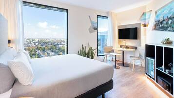 Quarto de hotel moderno com uma cama grande, uma escrivaninha, televisão e vista para a cidade.