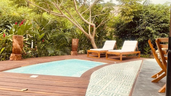 Um deck de madeira com uma pequena piscina, duas espreguiçadeiras e um tapete estampado.
