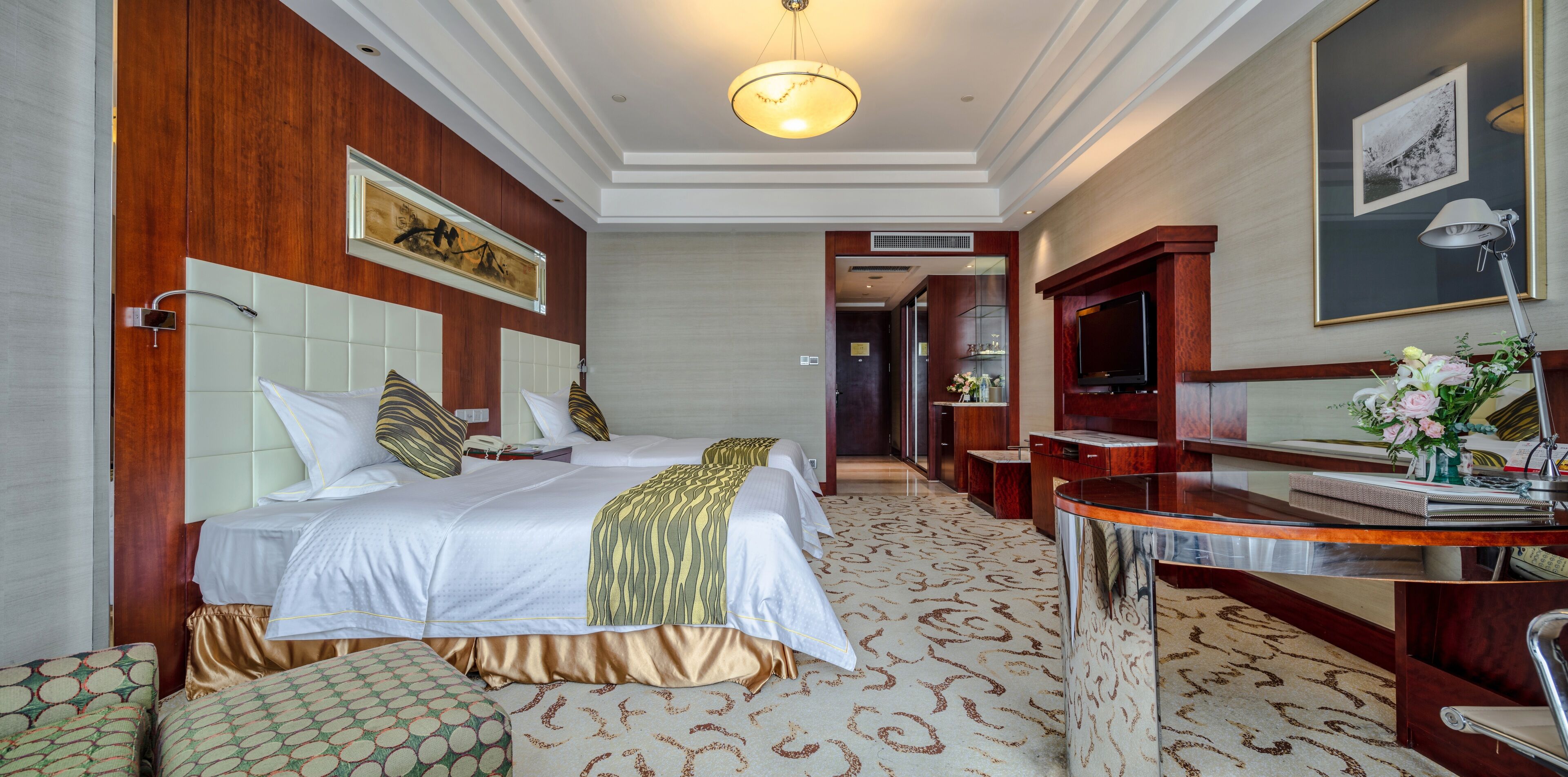 Quarto de hotel com uma cama grande, uma escrivaninha, um espelho e um banheiro visível por uma porta aberta.