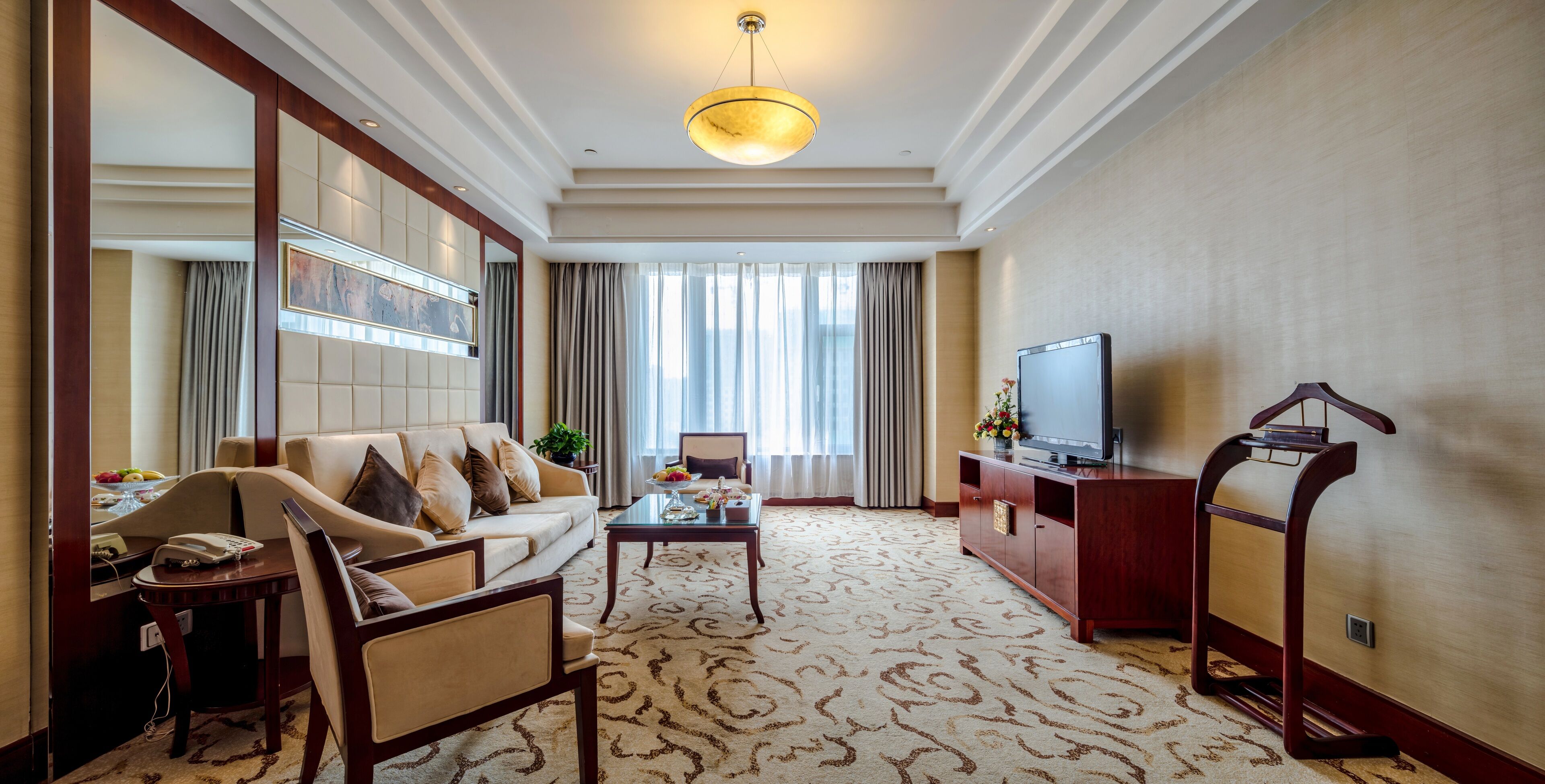 Quarto de hotel com sofá, poltronas, mesa de centro, televisão e guarda-roupa.