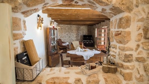 Um quarto rústico com paredes de pedra, teto de madeira, mesa de jantar com toalha de renda, cadeiras de couro e lareira.