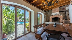 Um pátio com mesa e bancos de madeira, lareira de tijolos e piscina ao fundo.