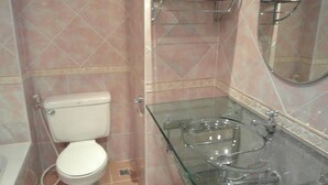 Casa de banho com sanita, lavatório de vidro e espelho.