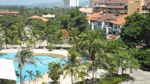 Um resort com piscina rodeada por palmeiras, uma praia e vista para edifícios altos ao fundo.